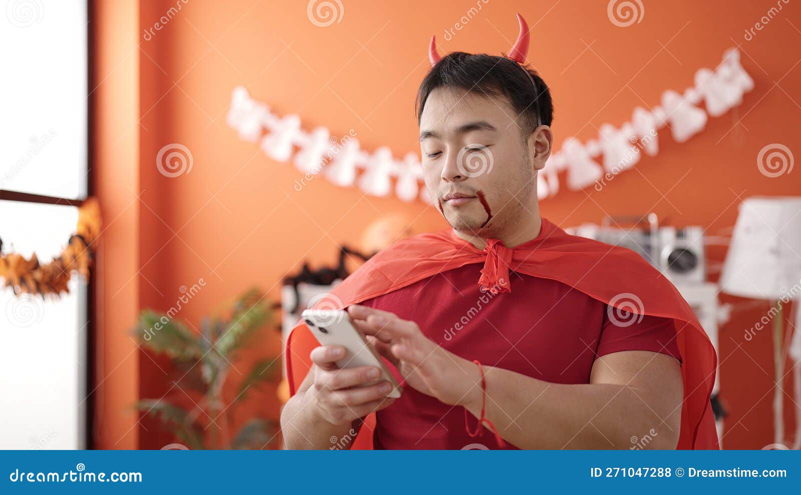 Young Chinese Man Wearing Devil Costume Using Smartphone at Home Stock ...