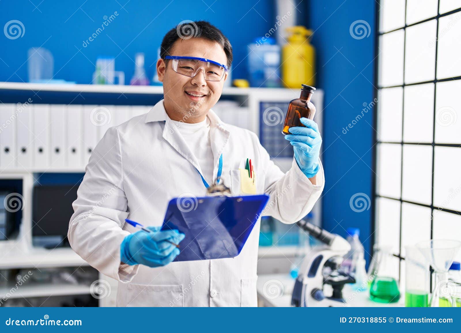 Young Chinese Man Wearing Scientist Uniform Reading Clipboard at ... Young Chinese Man Wearing Scientist Uniform Reading Clipboard at ...