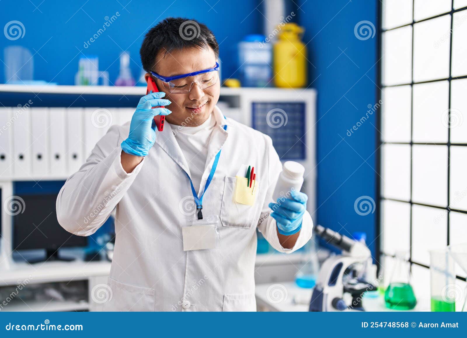 Young Chinese Man Wearing Scientist Uniform Using Smartphone at ... Young Chinese Man Wearing Scientist Uniform Using Smartphone at ...