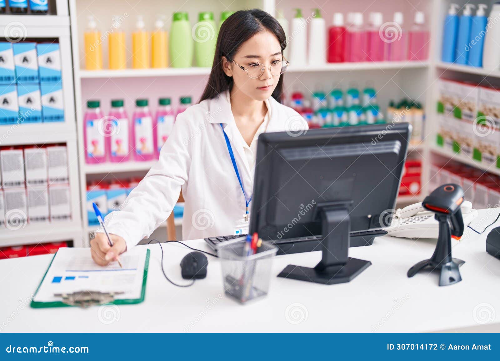 Young Chinese Woman Pharmacist Writing on Document Using Computer at ...