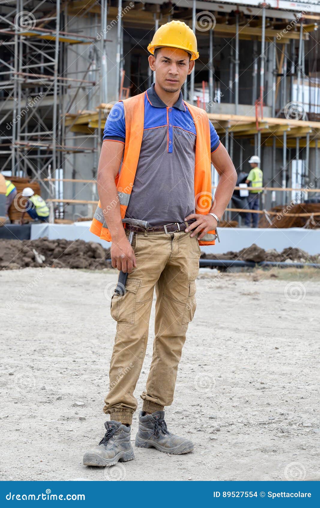 A Young Construction Worker Standing Watching An Excavator, Wearing A ...