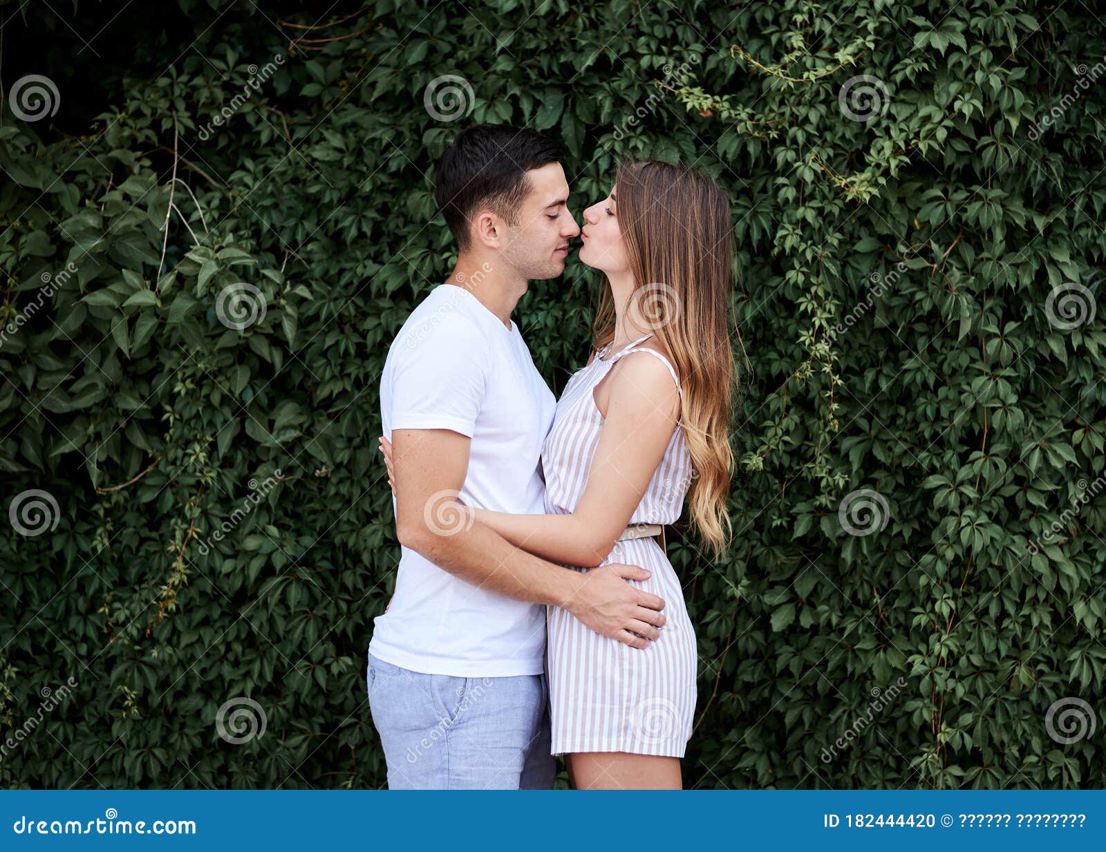 Young Couple In Love Hugging Kissing Near Green Bushes Trees Wall