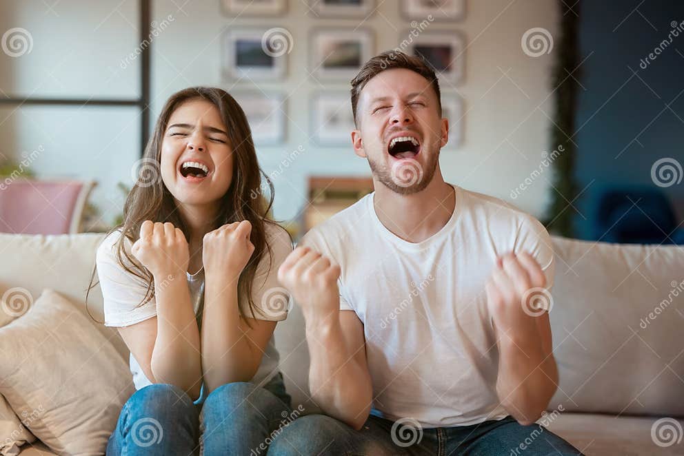 Young Couple Man And Woman Sitting On The Sofa Both Looking Winning