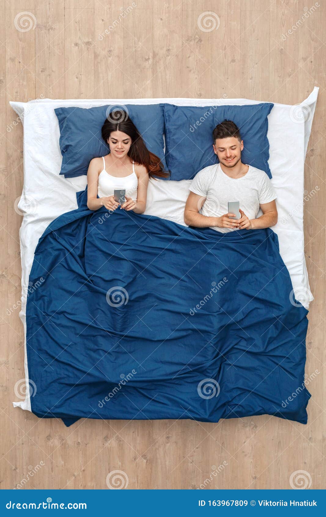 Bedtime Young Couple Lying Under Blanket On Bed Top View Chatting On