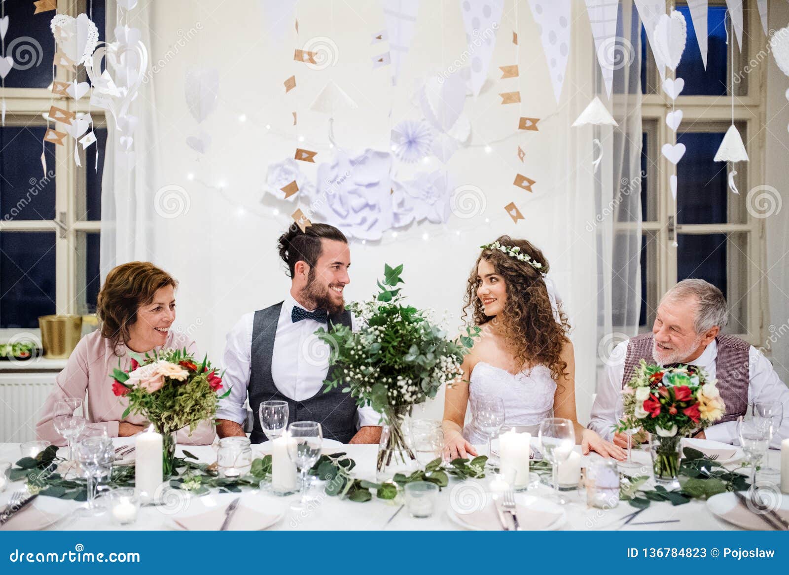 A Young Couple with Parents Sitting at a Table on a Wedding, Looking at ...