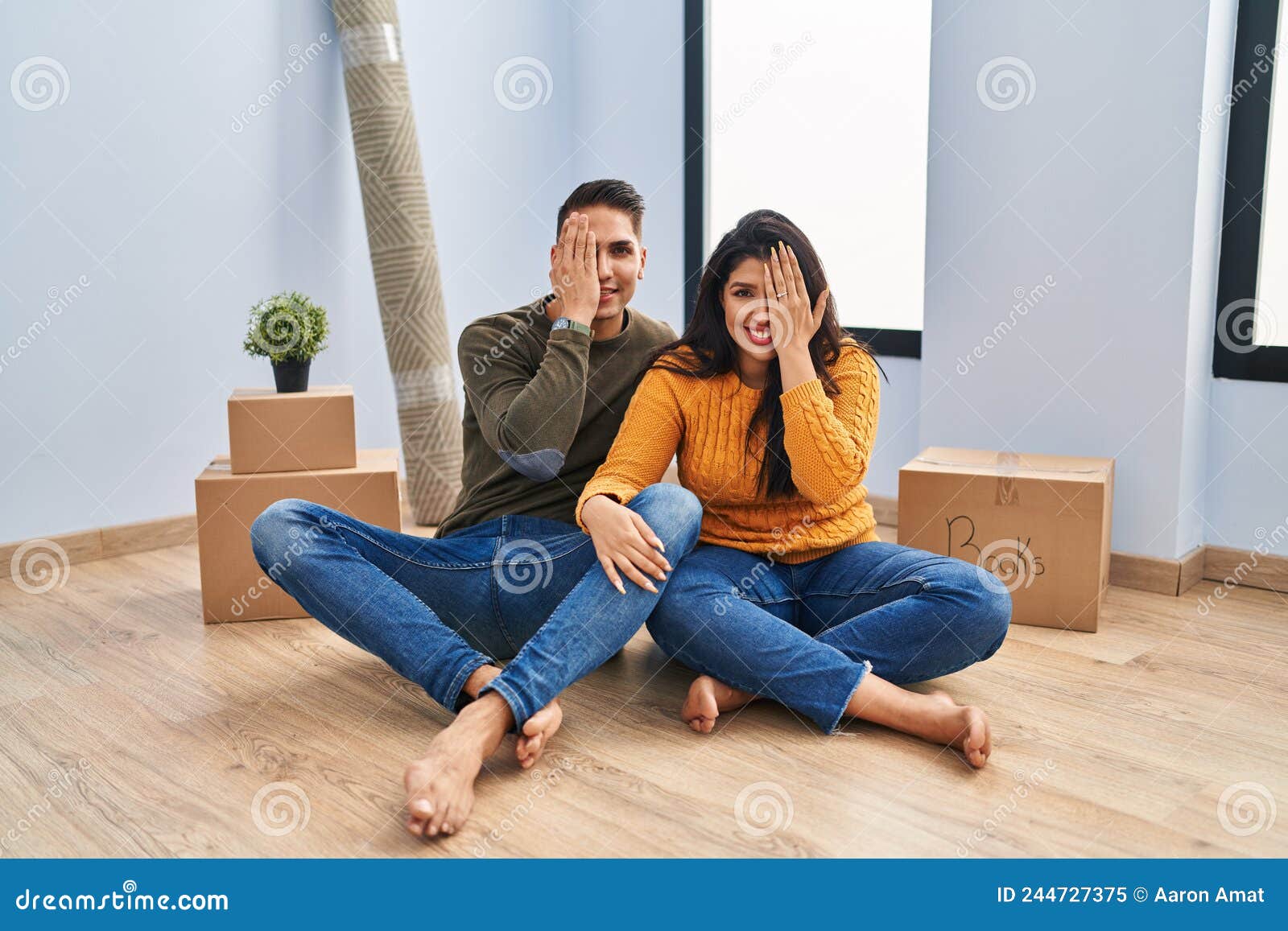 Young Couple Sitting On The Floor At New Home Covering One Eye With