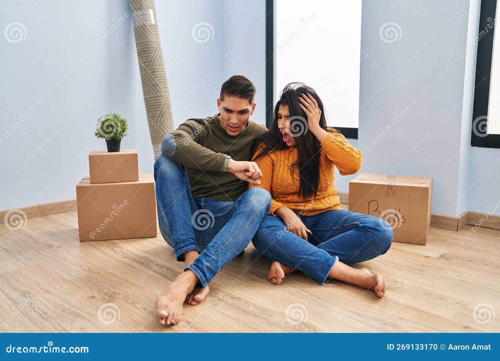 Young Couple Sitting On The Floor At New Home Looking At The Watch Time