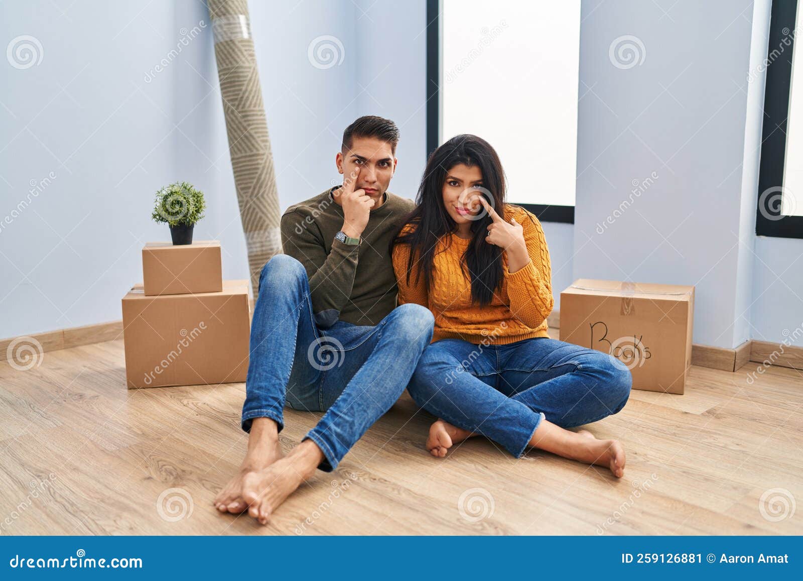 Young Couple Sitting On The Floor At New Home Pointing To The Eye