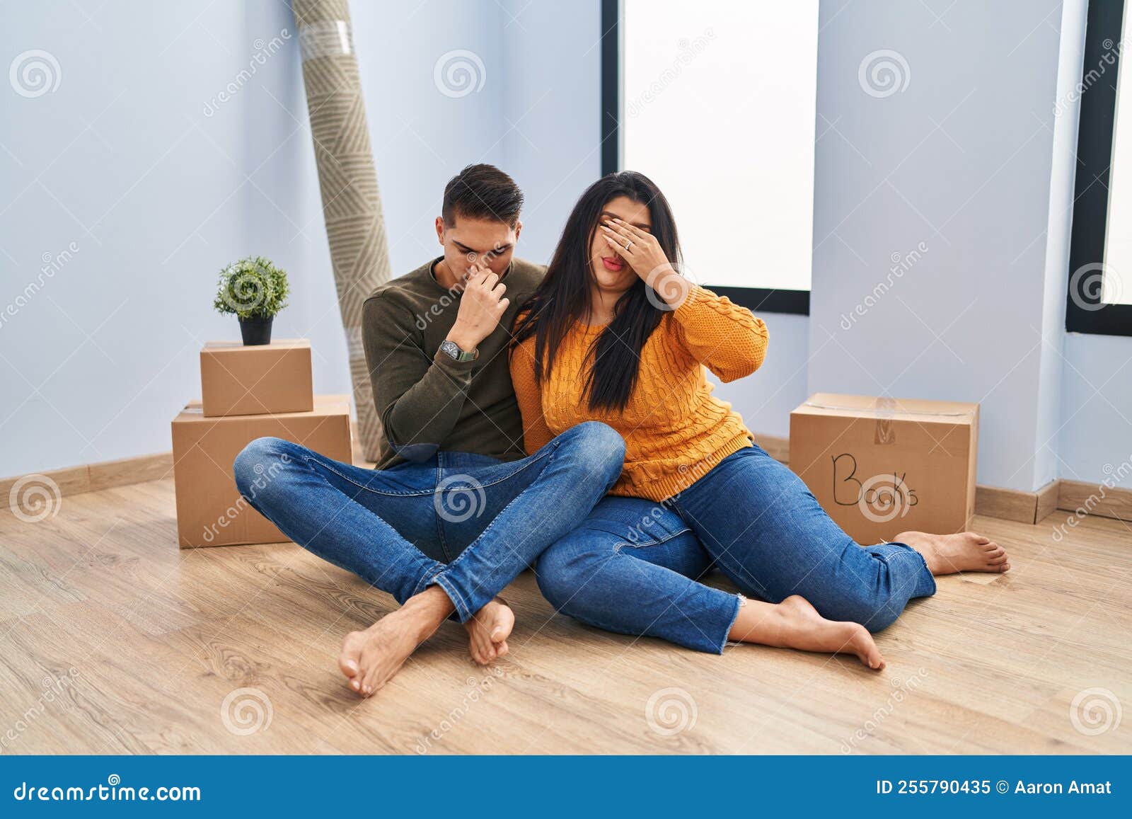 Young Couple Sitting On The Floor At New Home Tired Rubbing Nose And