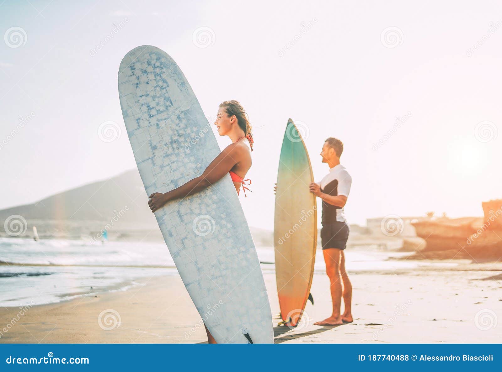 Young Couple Of Surfers Standing On The Beach With Surfboards Preparing