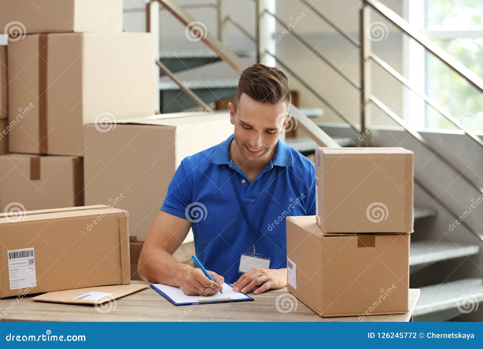 Young Courier Working with Papers among Parcels at Table Stock Photo ...