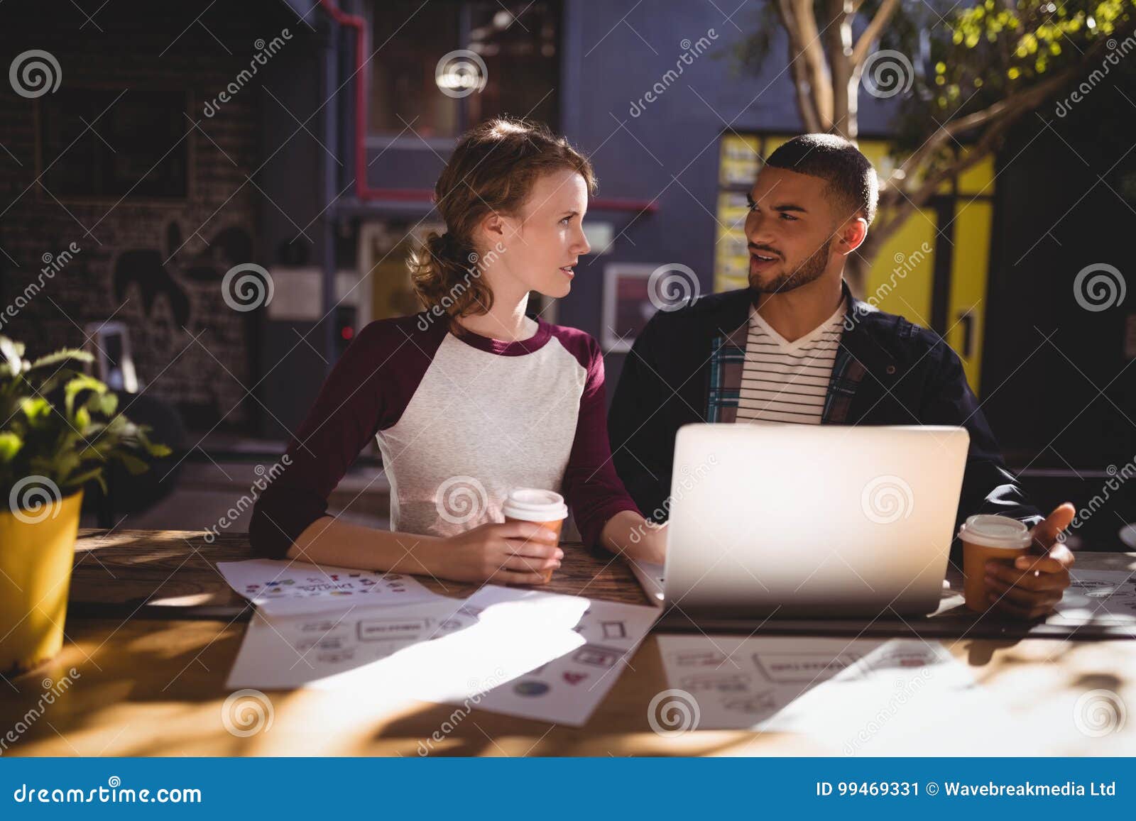 Young Creative Professionals Talking while Sitting with Laptop at ...