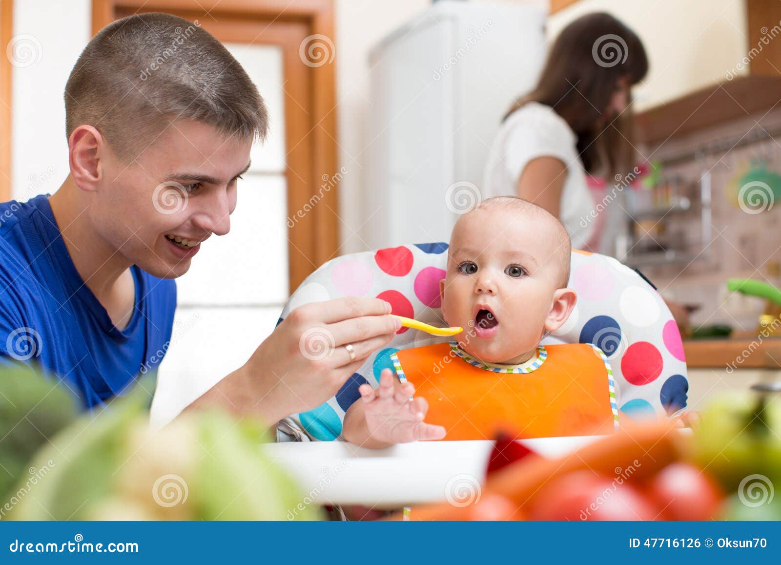 Young Dad Feeding Baby and Mom Cooking at Kitchen Stock Photo - Image ...