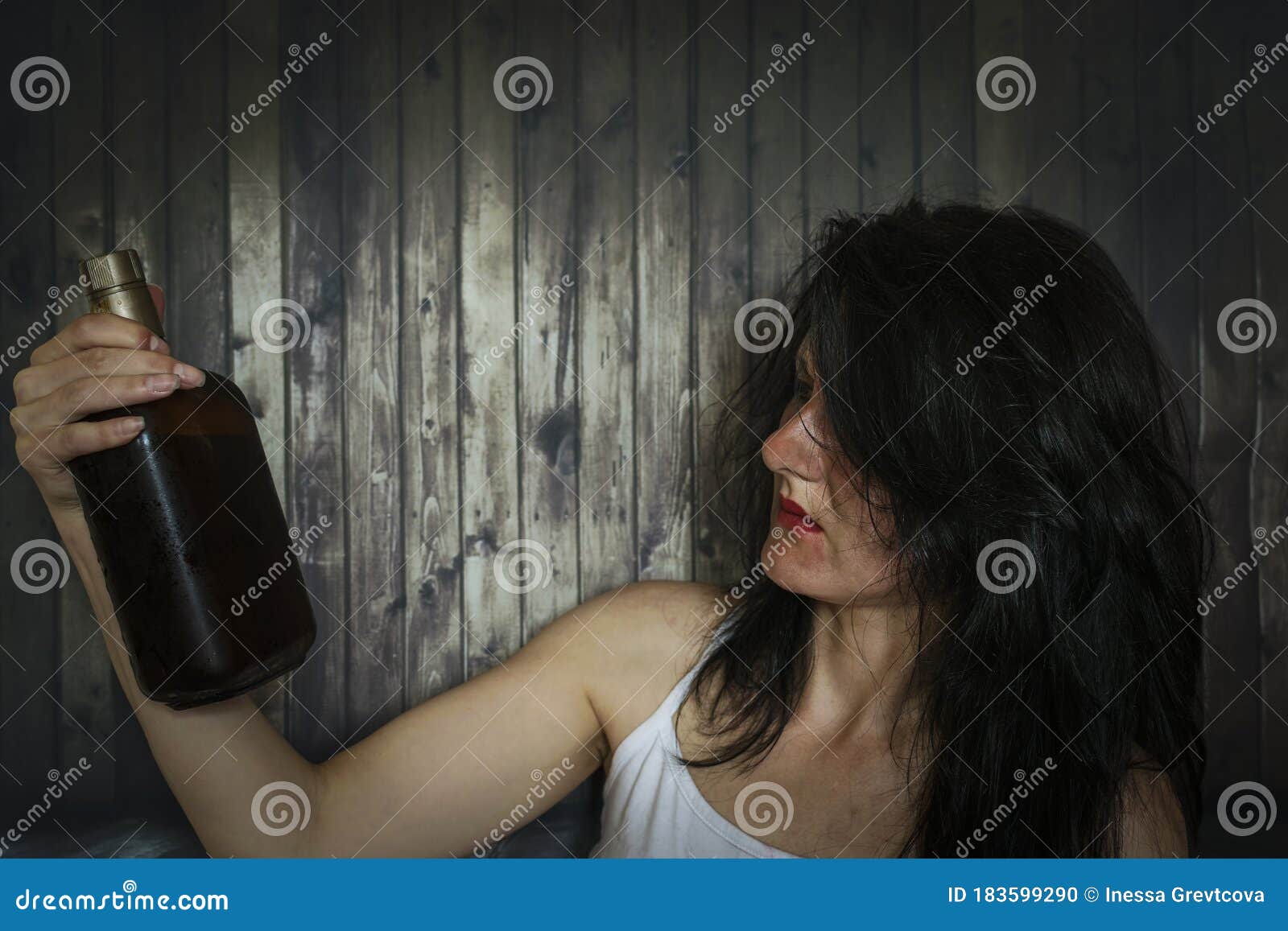 A Young Drunk Woman Looks At The Bottle Of Alcohol With Interest Stock