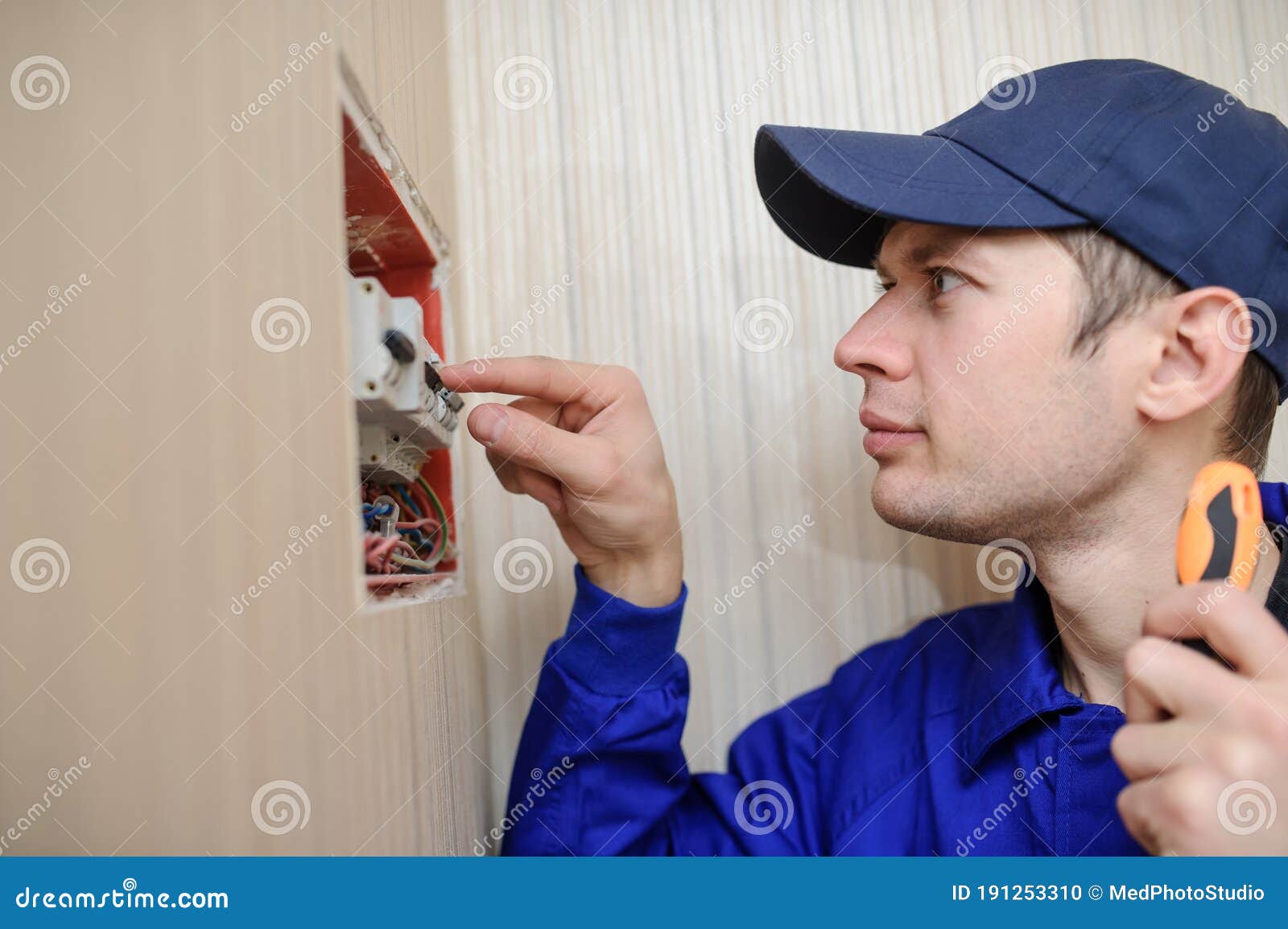 Young Electrician in Blue Overall Disassembling a Electrical Panel with ...