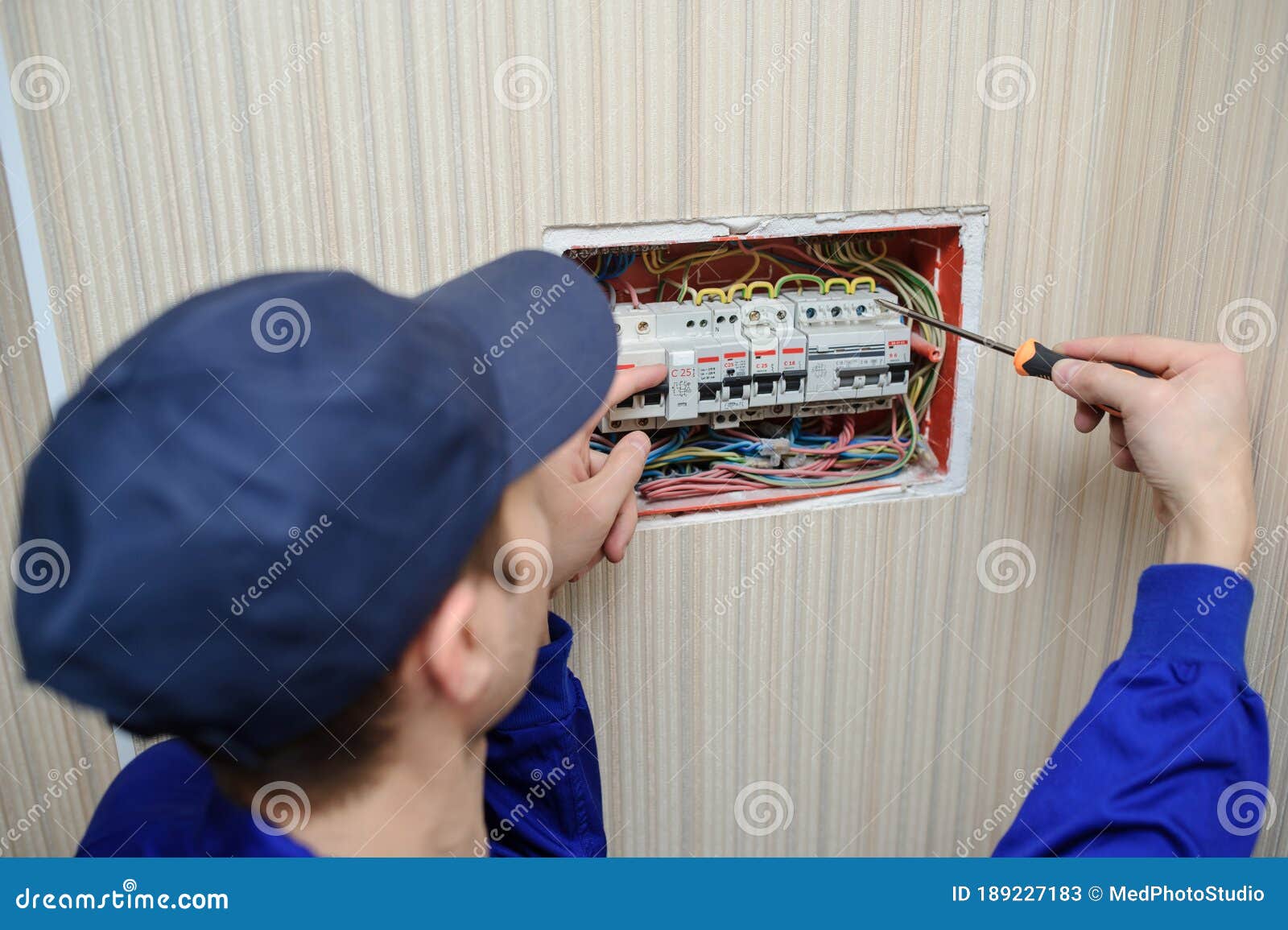 Young Electrician in Blue Overall Disassembling a Electrical Panel ...