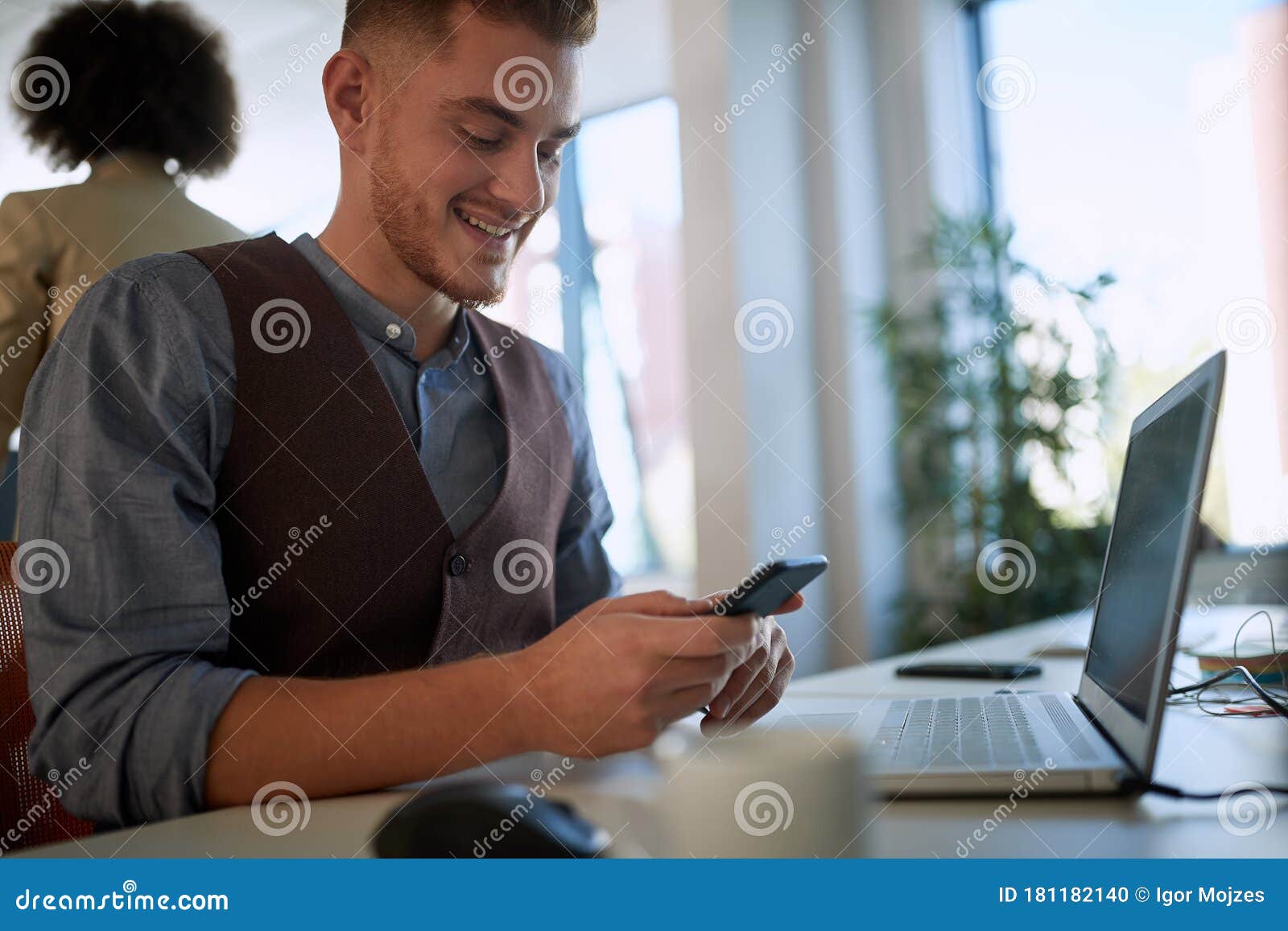 Young Employee Watching His Cell Phone, Smiling, on His Workplace in ...