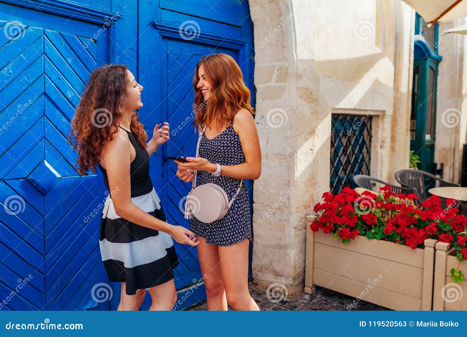 Young Female Friends Talking while Using Smartphone by Cafe. Happy ... Young Female Friends Talking while Using Smartphone by Cafe. Happy ...