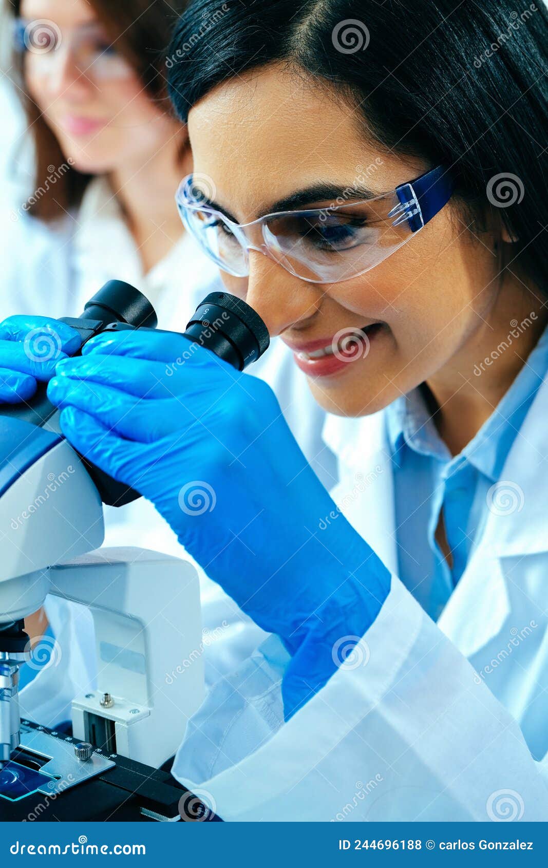 Young Female Scientist Using Microscope While Her Colleague Working In