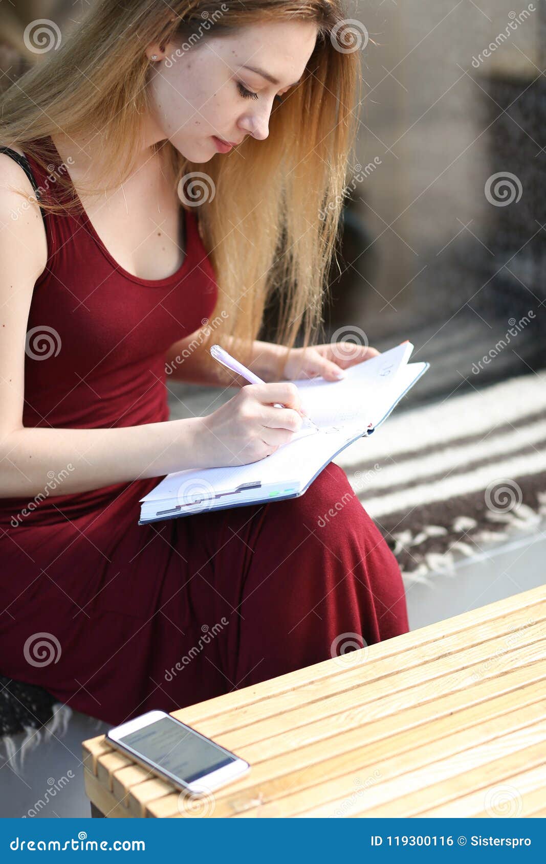 Young Female Student Writing Down in Notebook at University, Smartphone ...