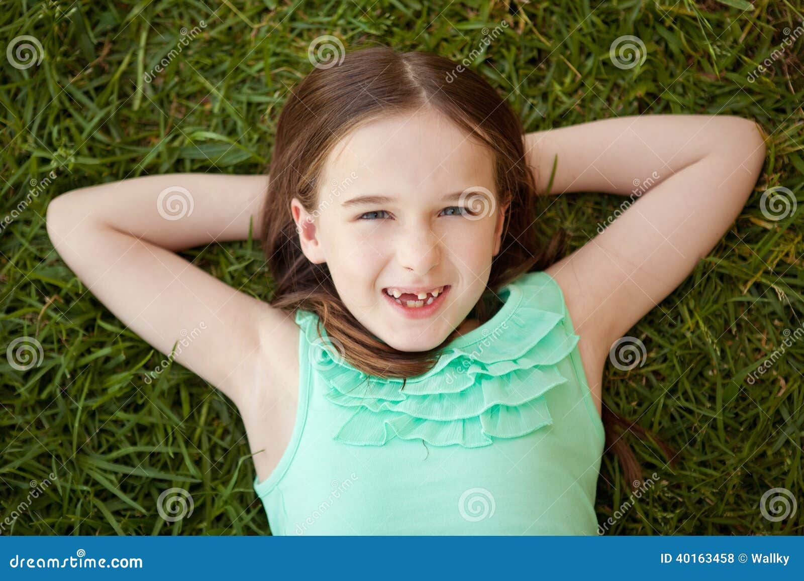 A Young Girl with a Missing Tooth is Lying on Her Back on the Grass ...