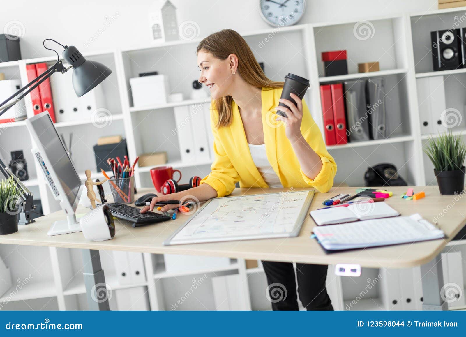 A Young Girl Stands Near A Table Looks At The Monitor And Holds A
