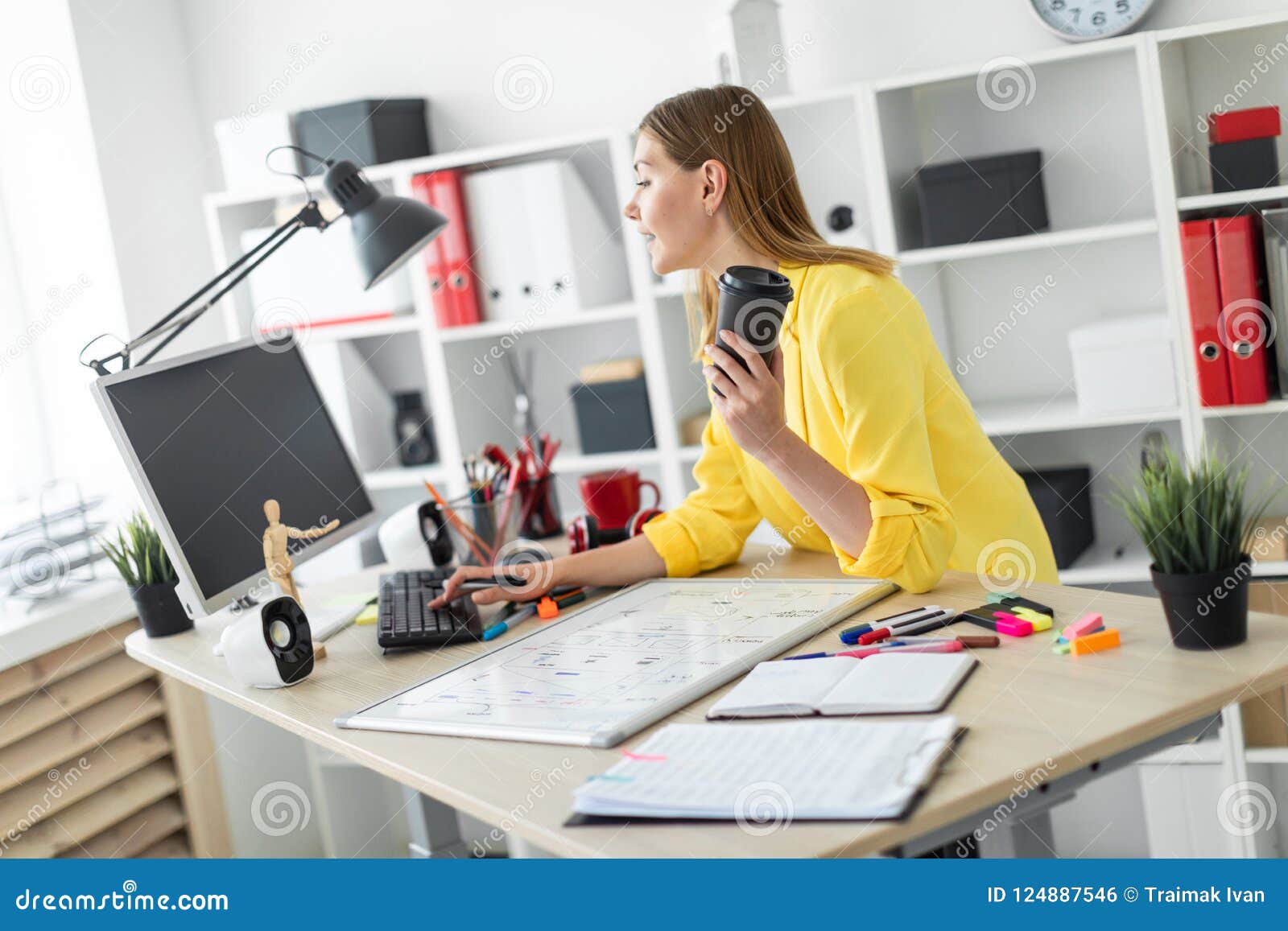 A Young Girl Stands Near A Table Looks At The Monitor And Holds A