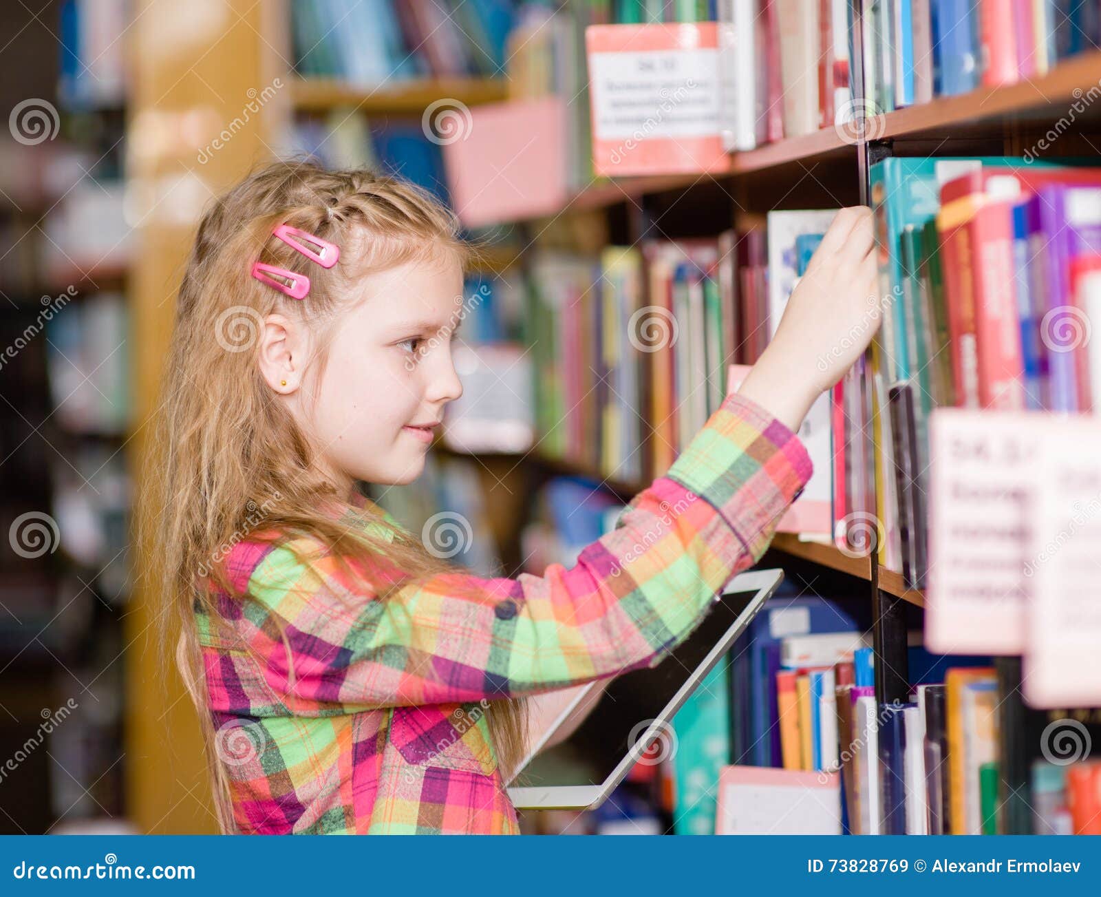 Young Girl with Tablet Computer Chooses a Book in the Library Stock ...