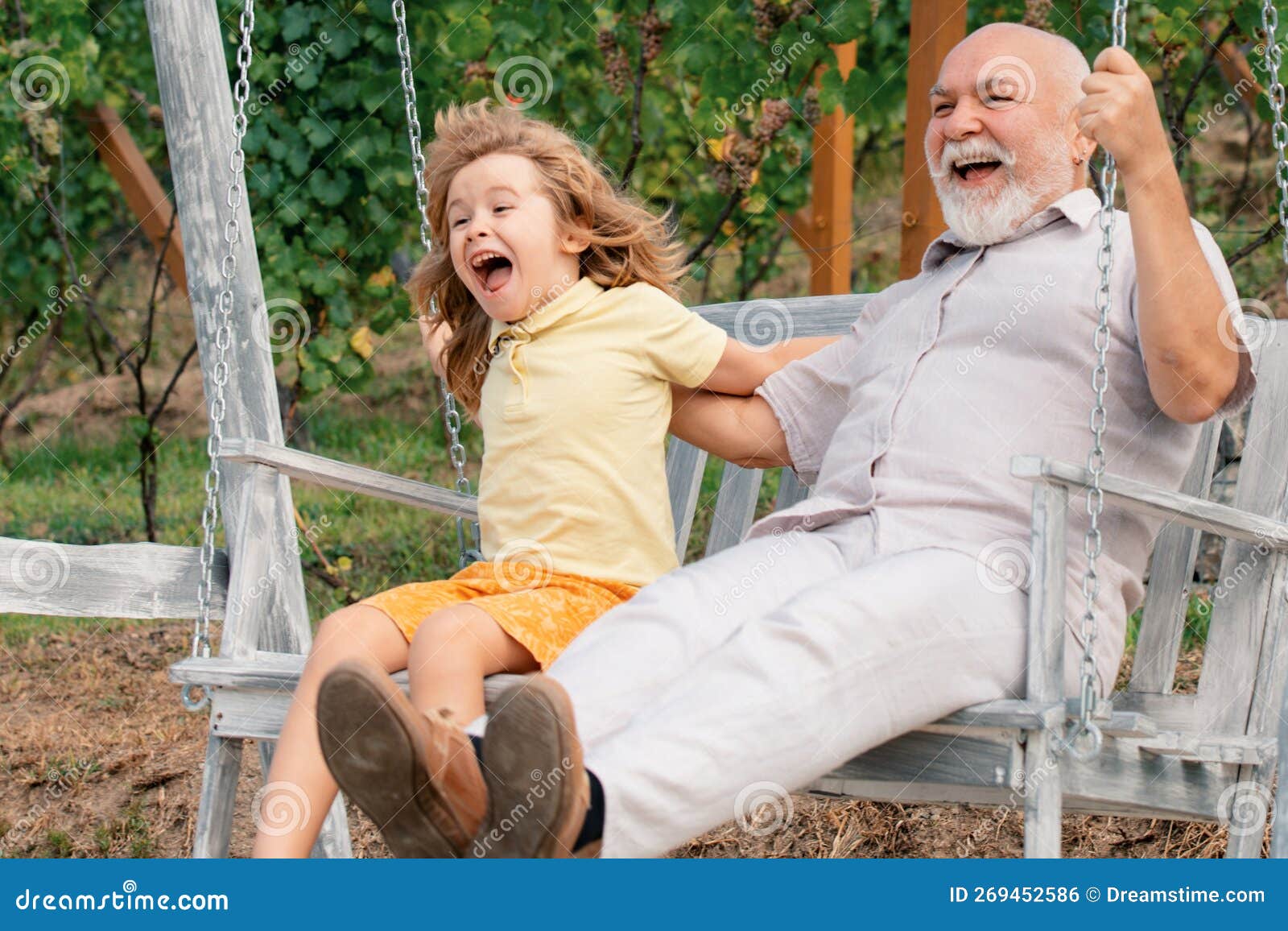 Young Grandson And Old Grandfather Swinging In Spring Garden Grand Dad