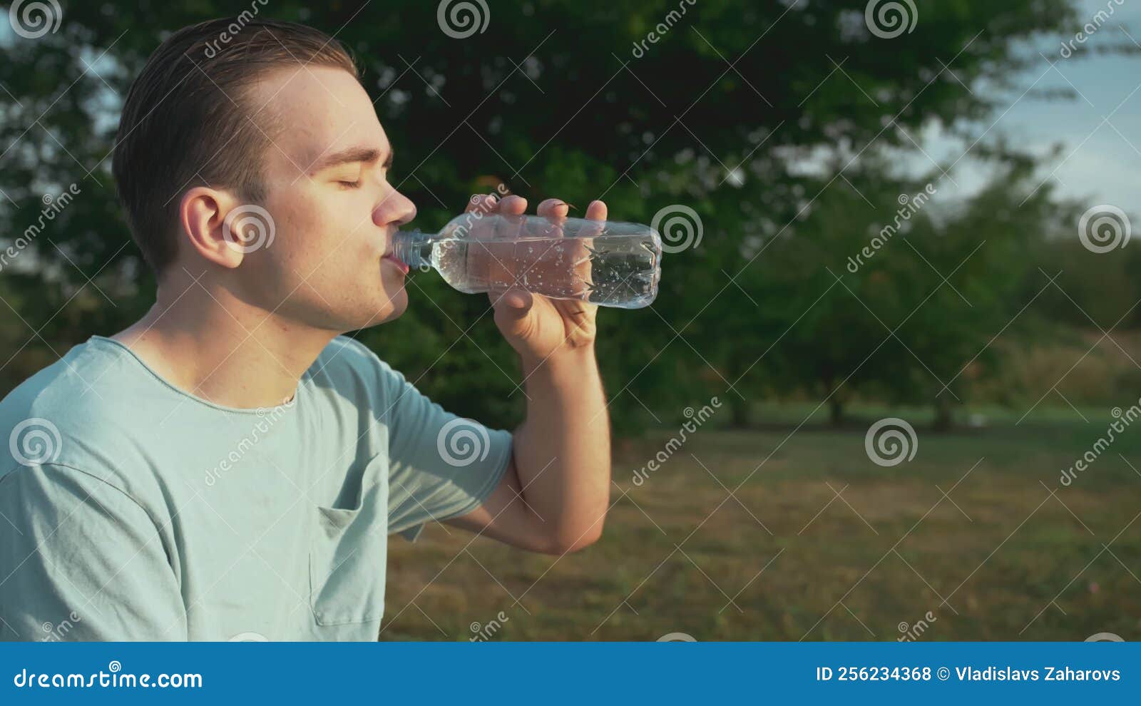 A Young Guy Drinks Water from a Bottle, on the Background of a Lake ...