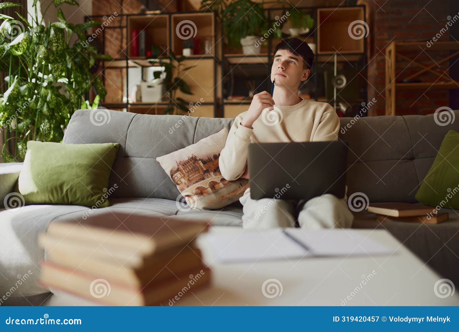 Young Guy Siting on Sofa at Home with Laptop and Doing Homework. Man ...
