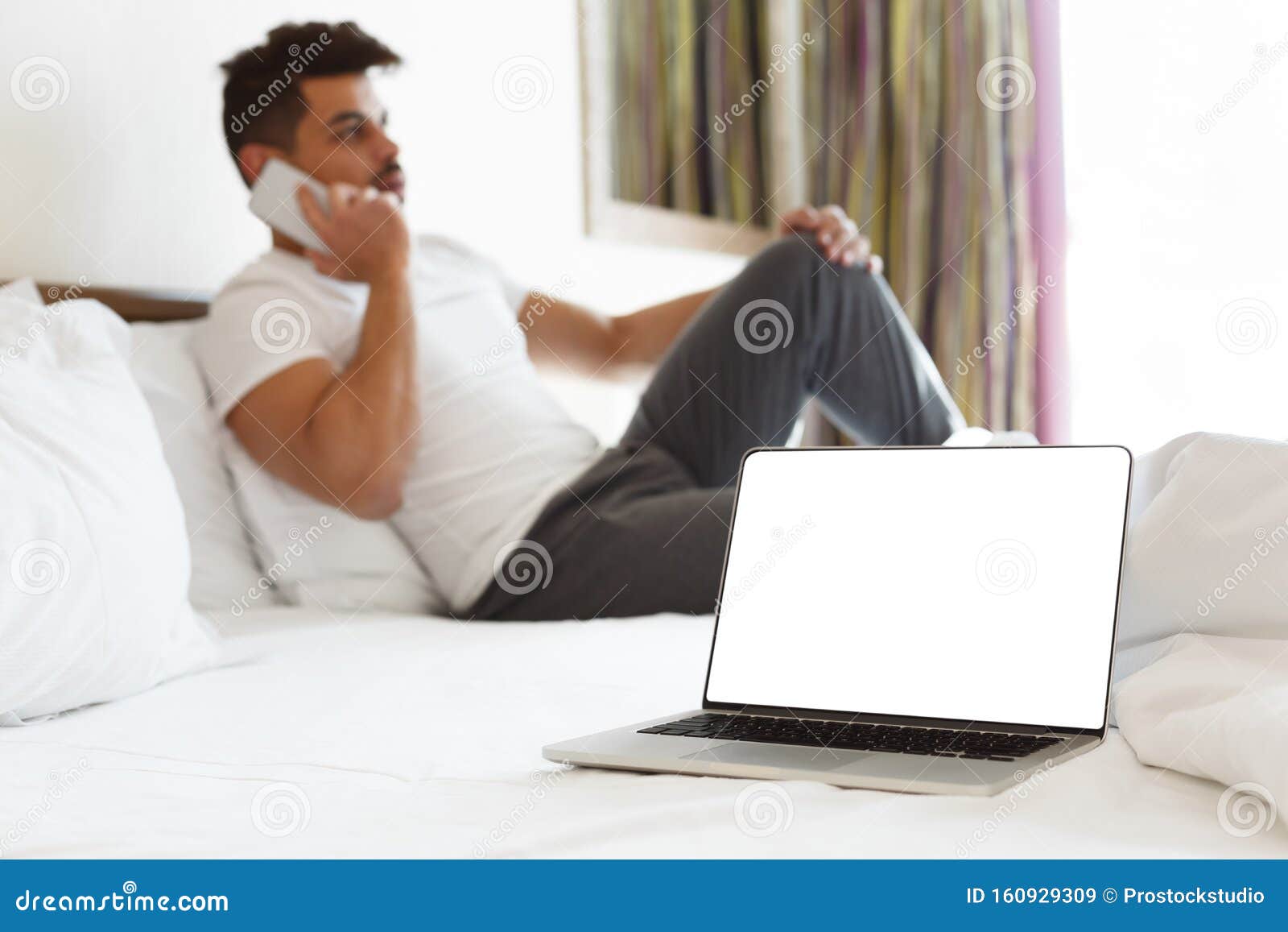 Young Guy Using Laptop with Blank Screen, Talking by Phone in Bed Stock ...