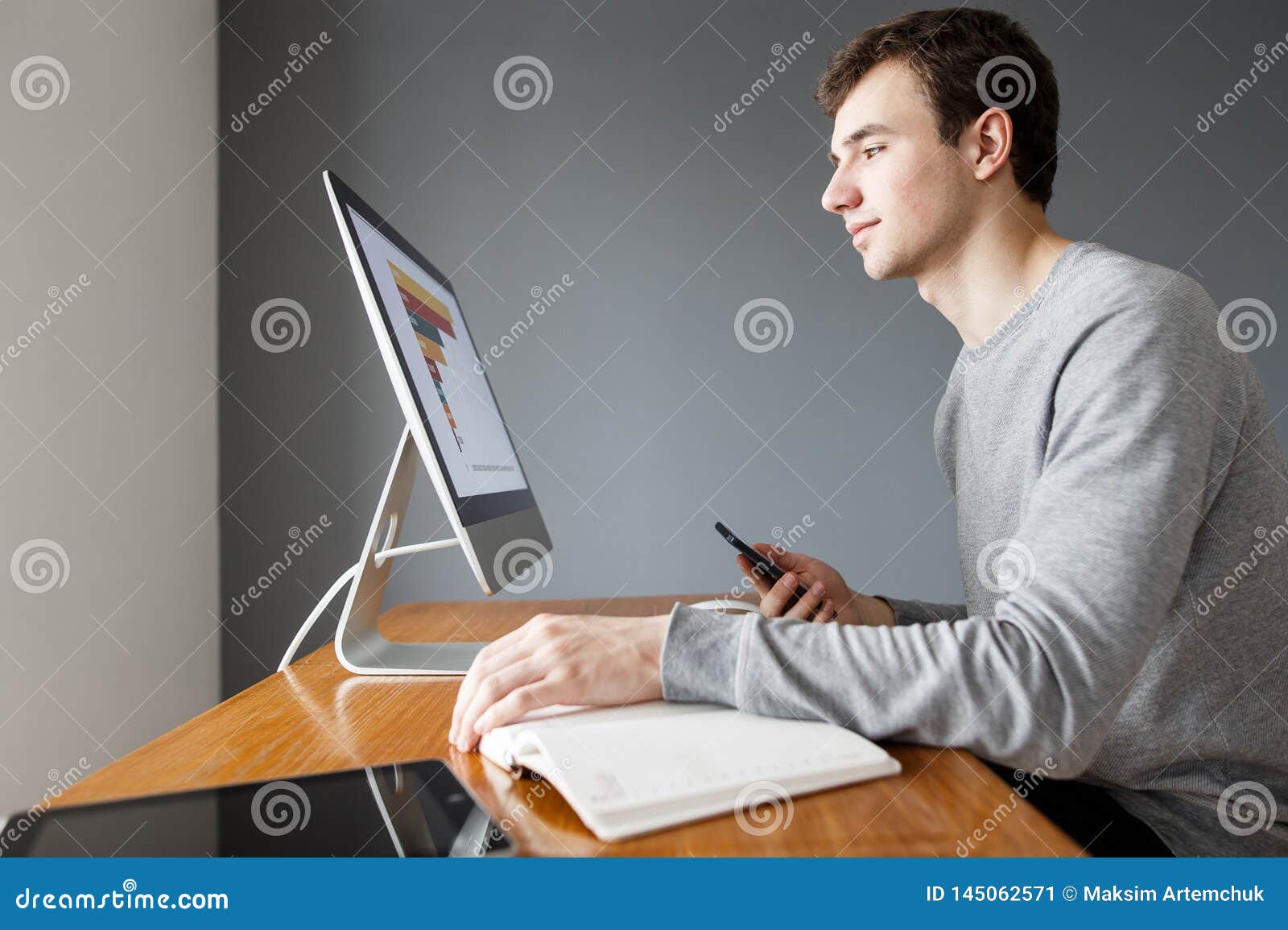 A Young Handsome Guy Sits at a Table and Looks at the Computer Screen ...