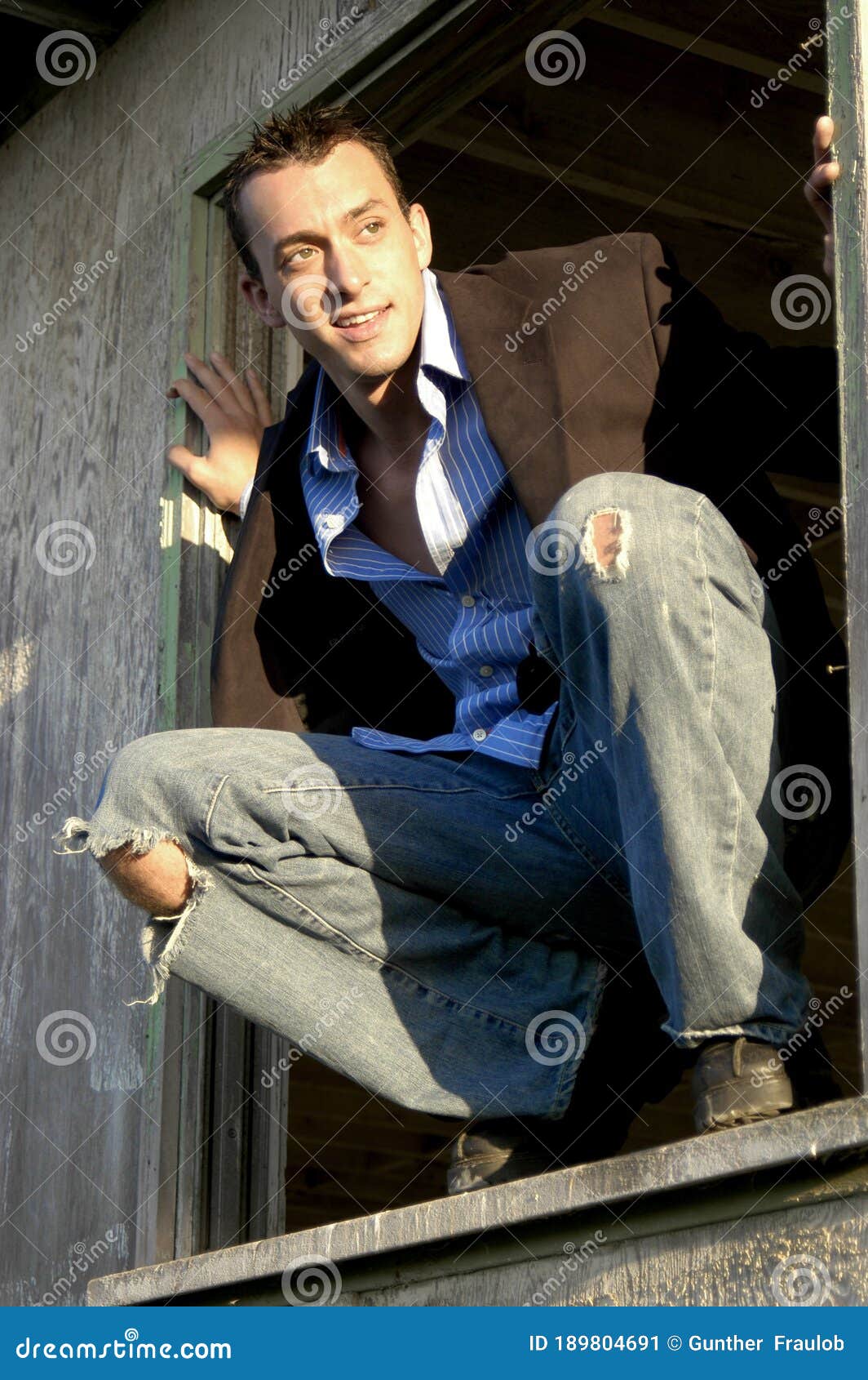 Young Handsome Man Crouching on a Window Ledge of a Broken Down Barn on ...