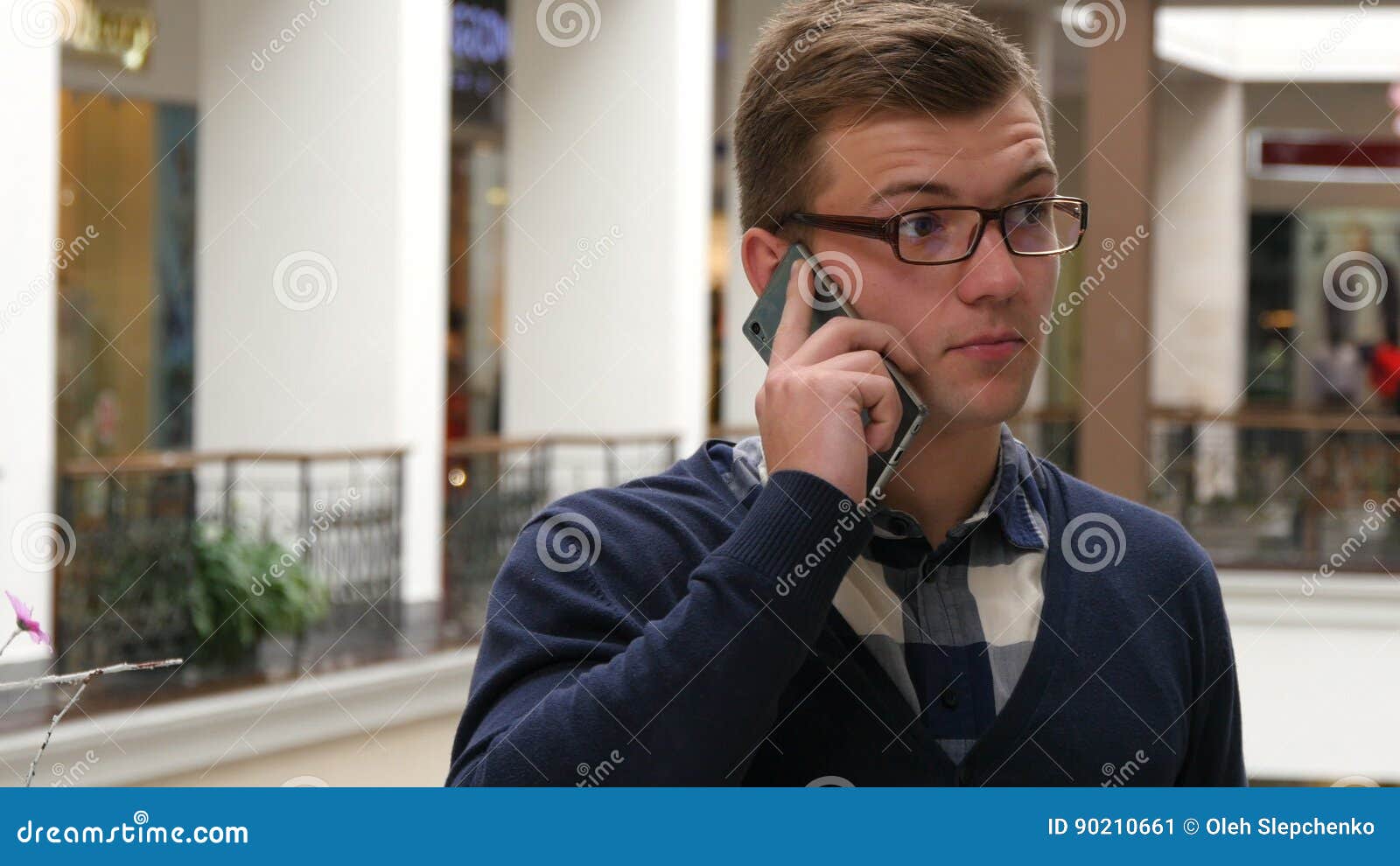 Young Handsome Man In Glasses Talking On The Cellphone In Shopping Mall