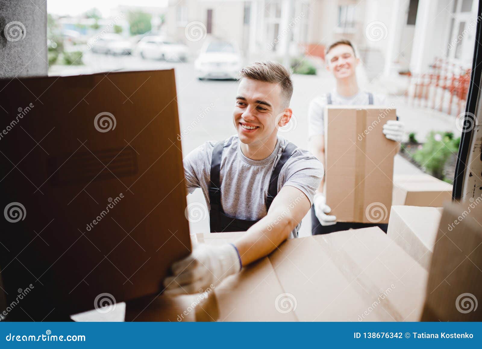 A Young Handsome Smiling Mover Wearing Uniform is Reaching for the Box ...