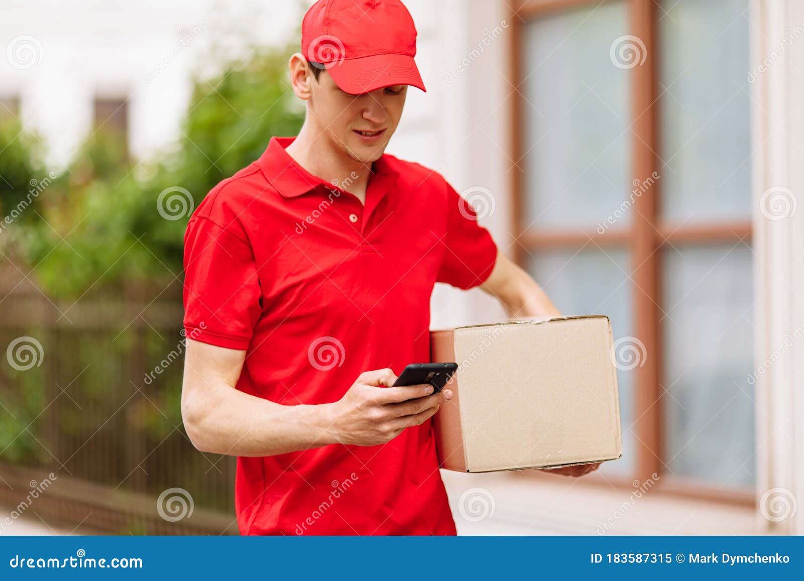 Courier with a Cardboard Box, Using a Mobile Phone. Home Delivery Stock ...
