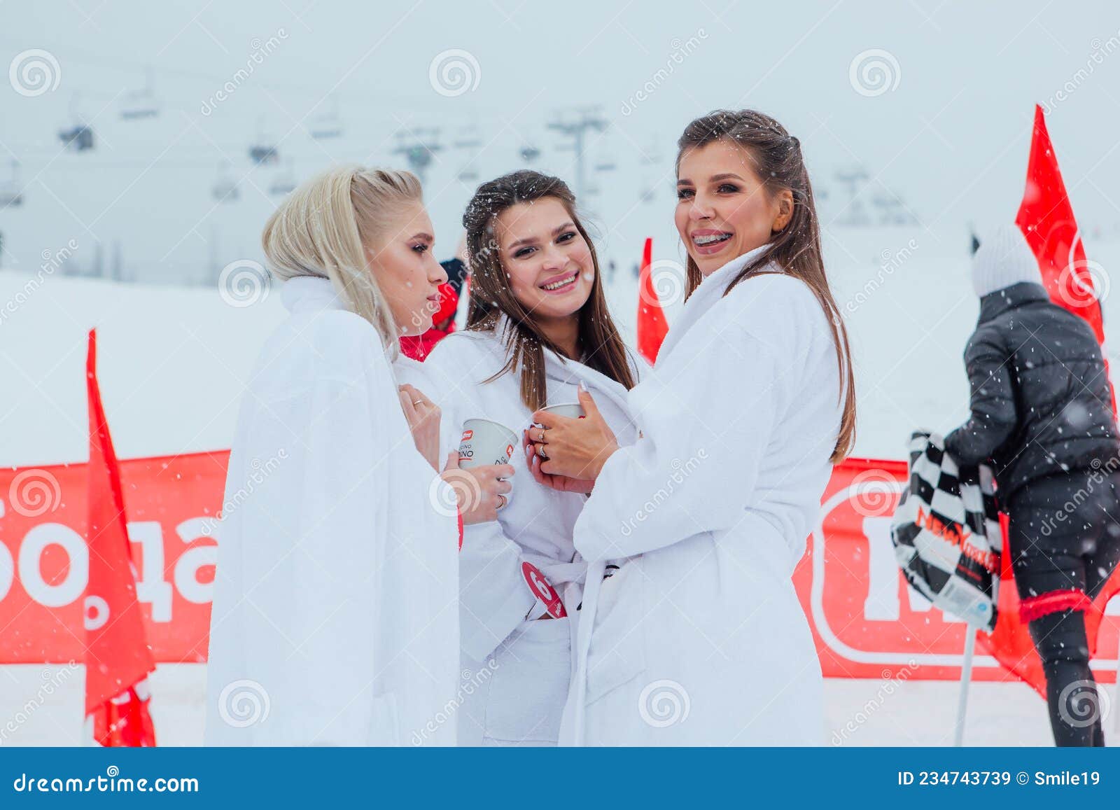 Young Happy Pretty Women In Red Bikinis And White Bathrobes On The Snow