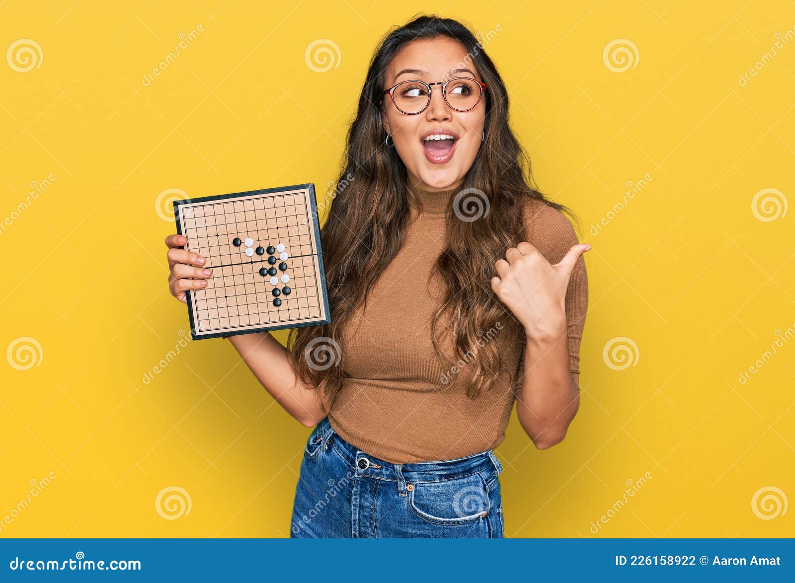 Young Hispanic Girl Holding Drauhgts Pointing Thumb Up To The Side