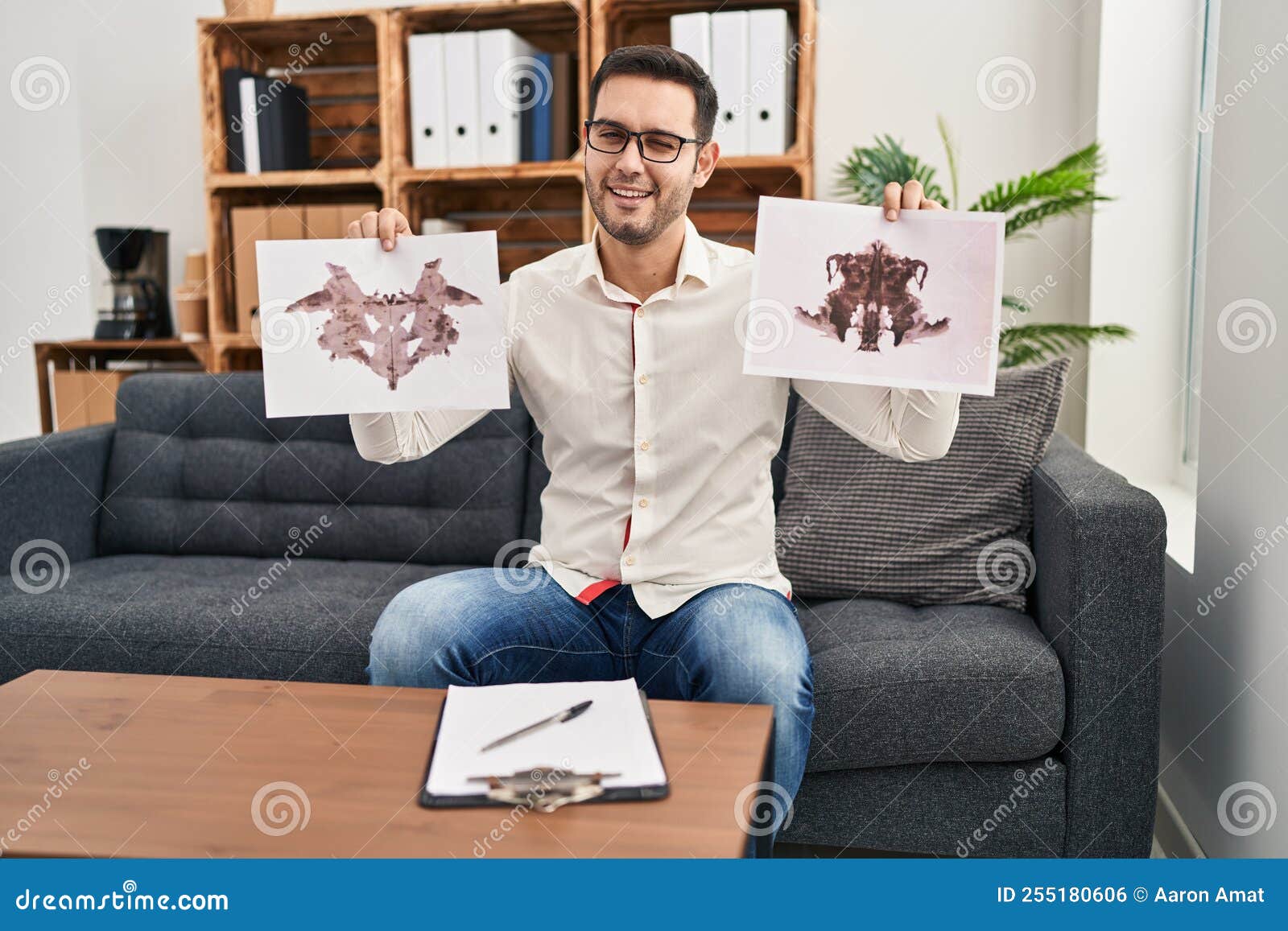 Young Hispanic Man With Beard Holding Rorschach Test Winking Looking At