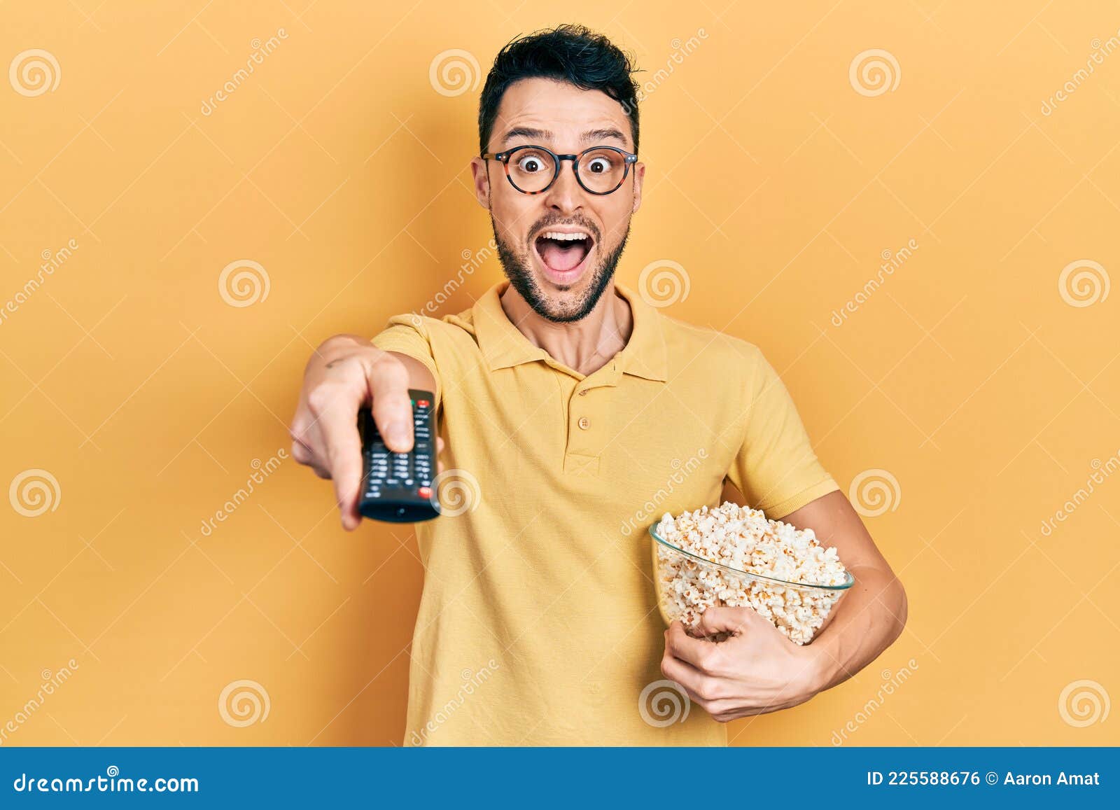Young Hispanic Man Eating Popcorn Using Tv Control Celebrating Crazy