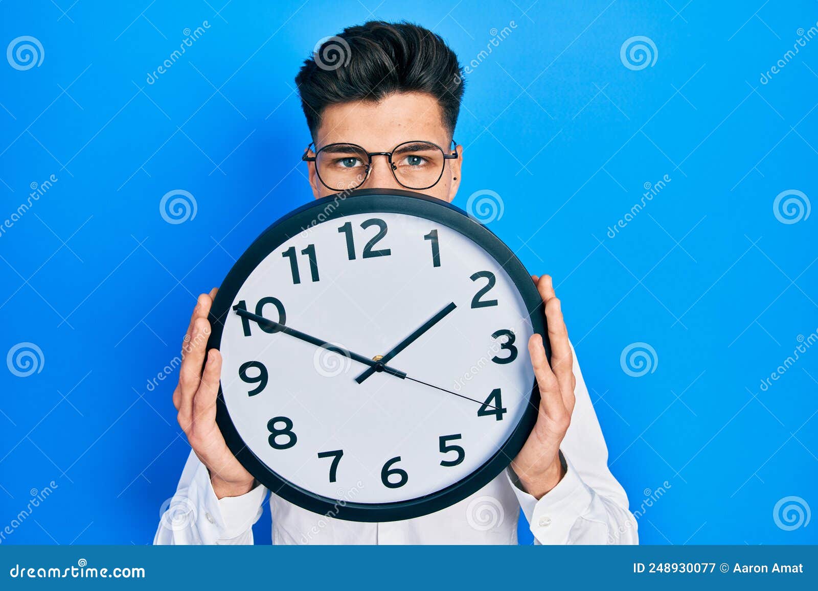 Young Hispanic Man Holding Big Clock Over Face Relaxed with Serious ...