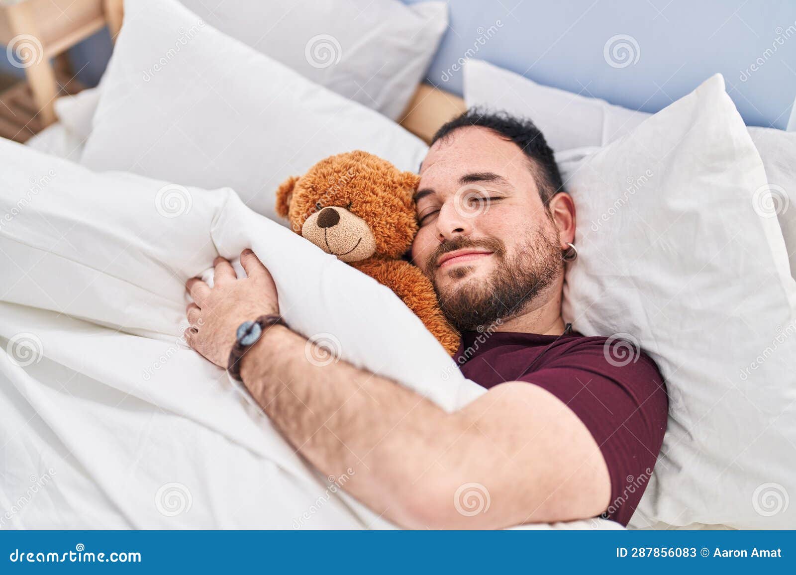 Young Hispanic Man Hugging Teddy Bear Lying On Bed Sleeping At Bedroom