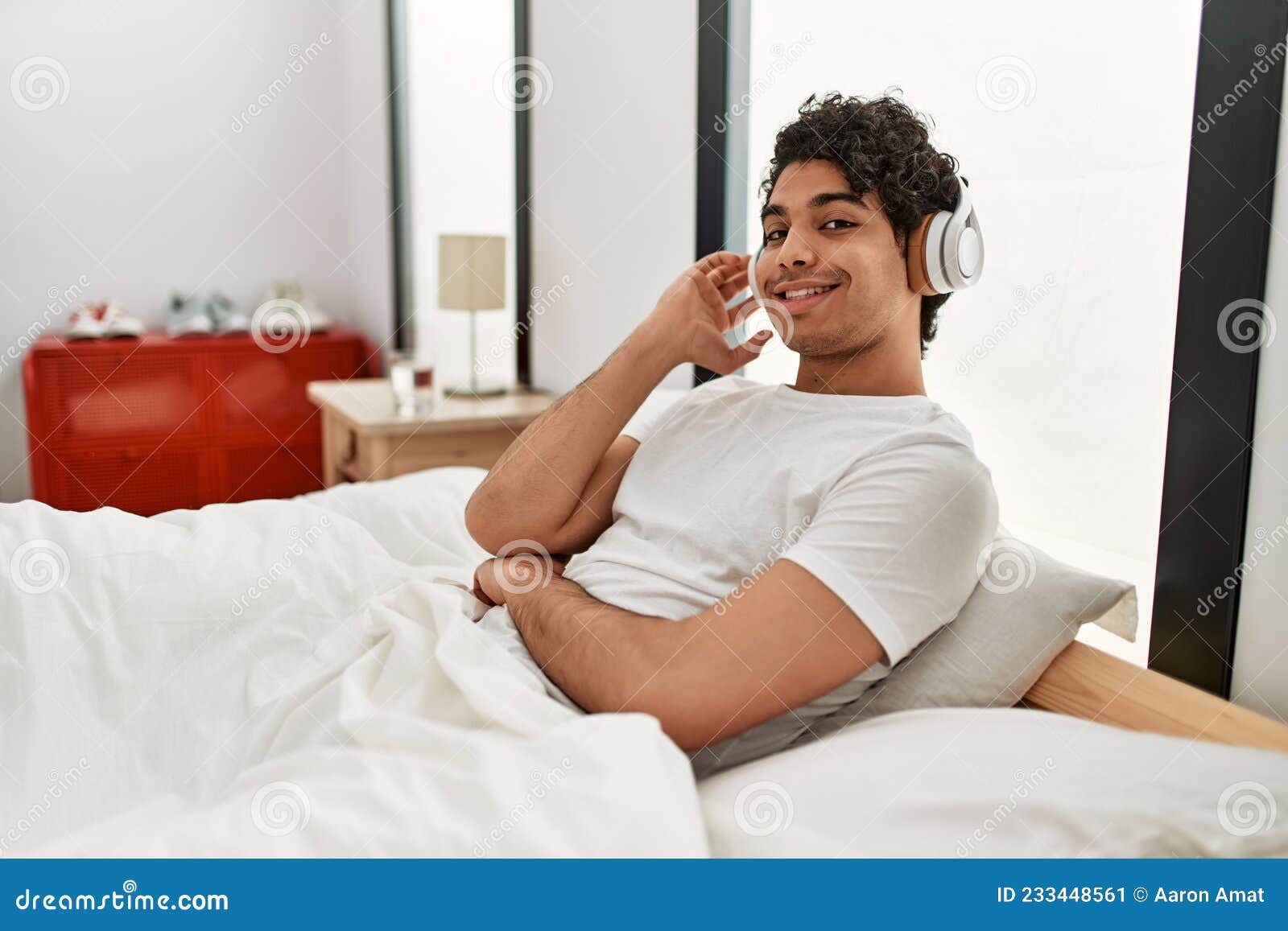 Young Hispanic Man Listening To Music Sitting On The Bed At Bedroom