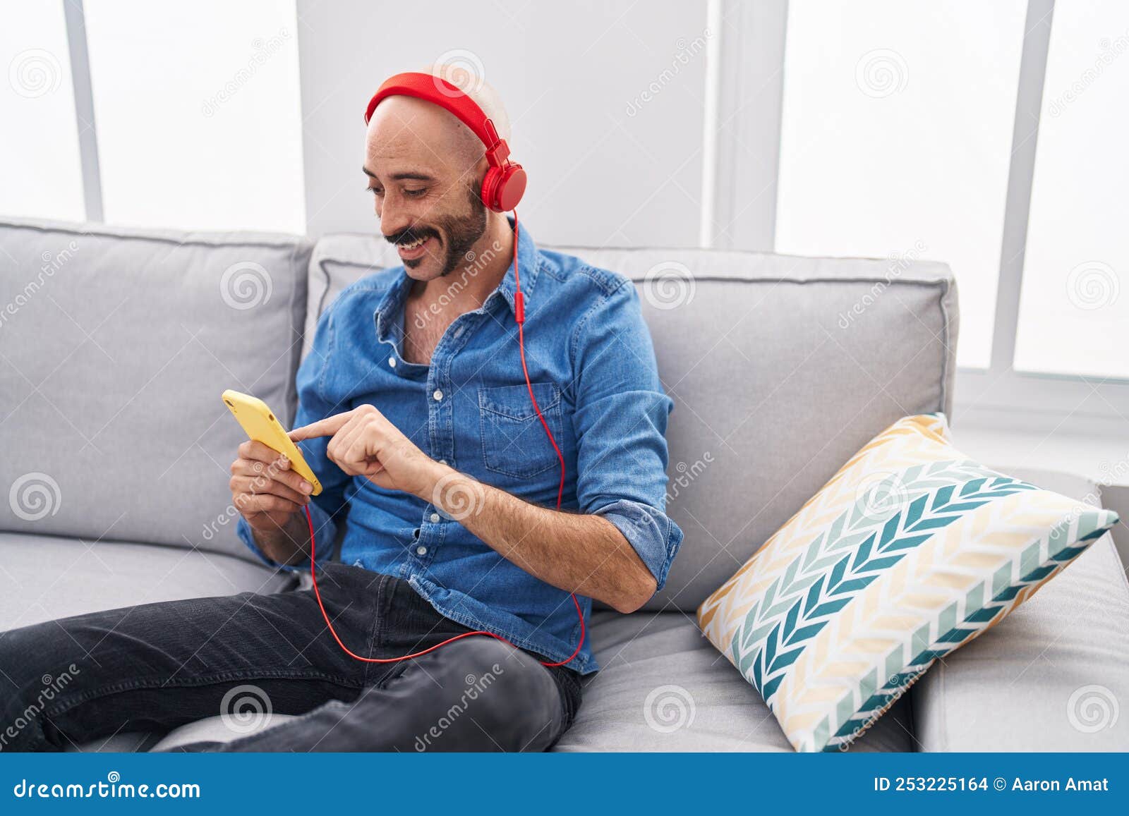 Young Hispanic Man Listening To Music Sitting On Sofa At Home Stock
