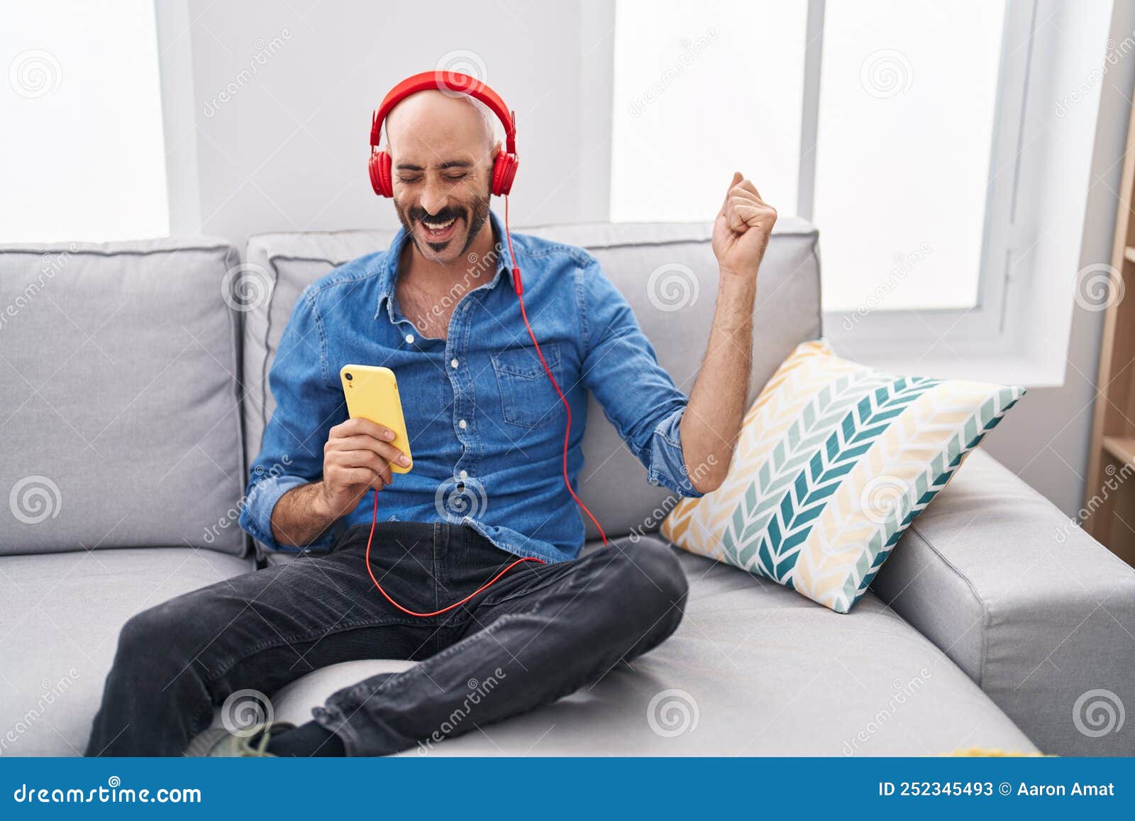 Young Hispanic Man Listening To Music Sitting On Sofa At Home Stock
