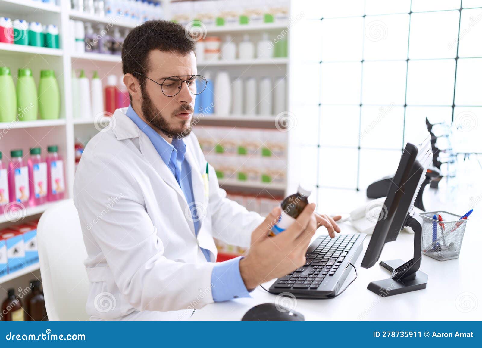 Young Hispanic Man Pharmacist Using Computer Holding Medication Bottle ...