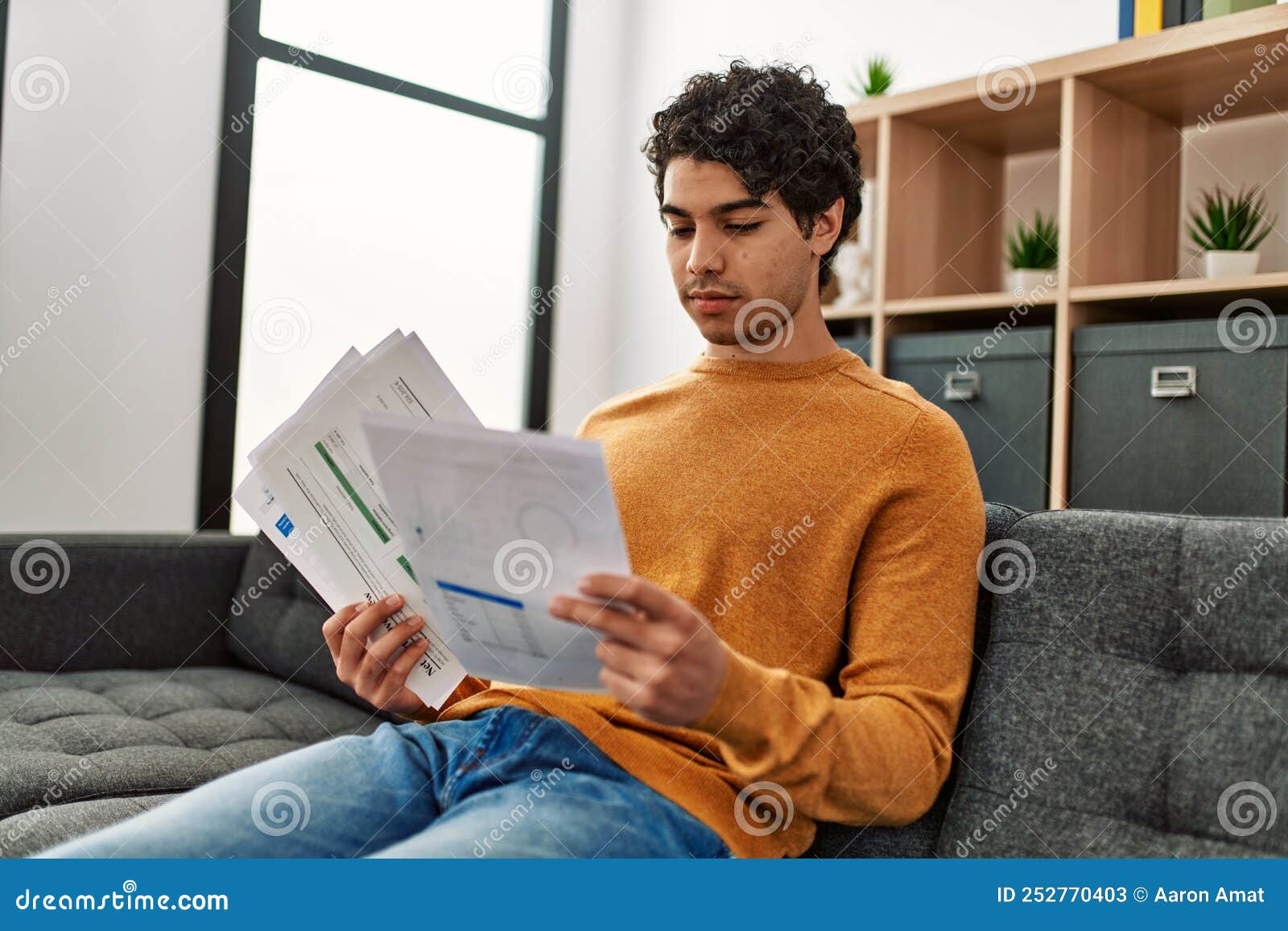 Young Hispanic Man Reading Paperwork Sitting on the Sofa at Home Stock ...