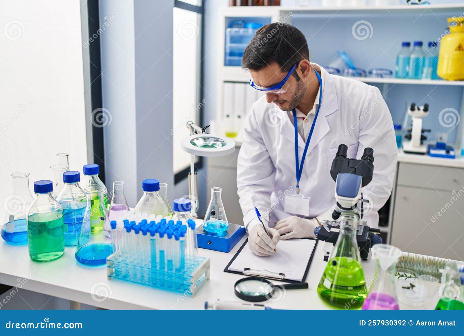 Young Hispanic Man Scientist Measuring Liquid Writing Report at ...