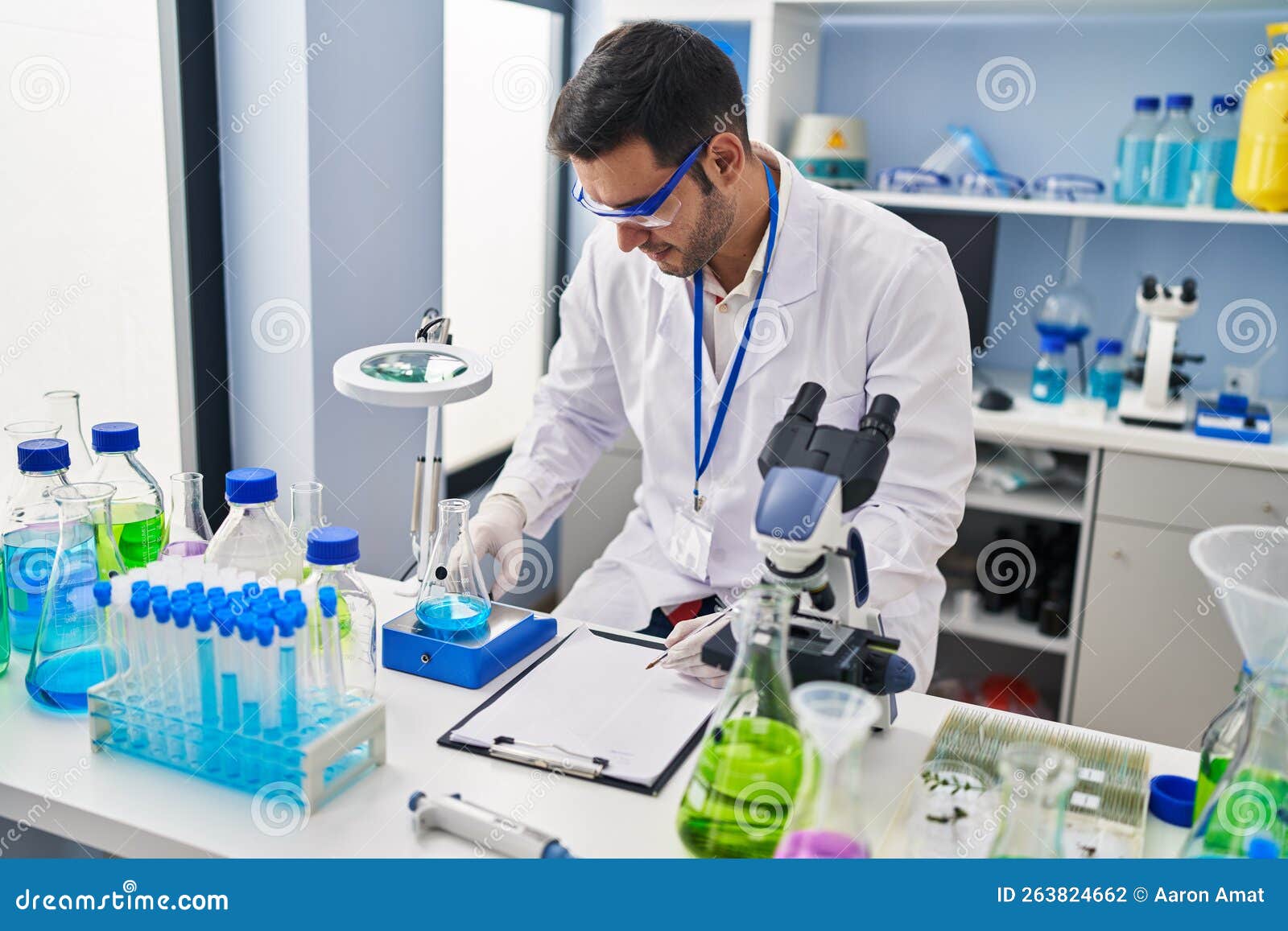 Young Hispanic Man Scientist Measuring Liquid Writing Report at ...